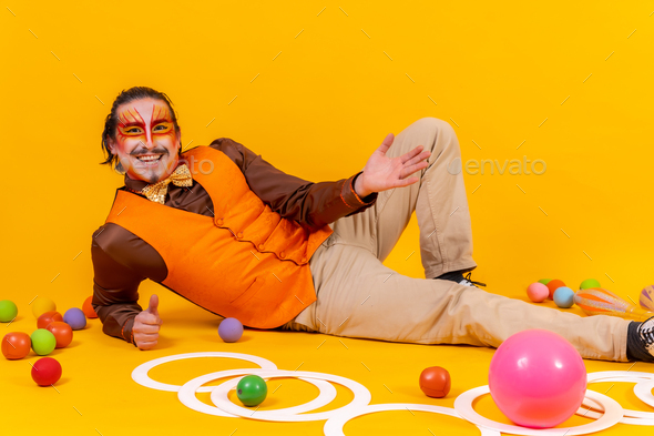 Juggler in a vest and with a painted face lying with the juggling ...