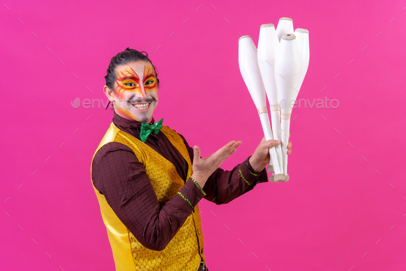 Juggler in a vest and with painted face juggling maces on a pink ...