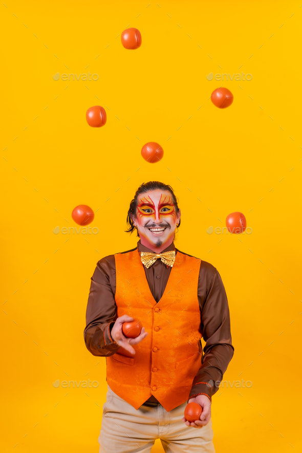 Juggler in a vest and with a painted face juggling balls on a yellow ...