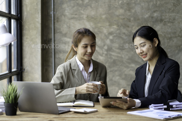 Smiling young Asian businesswomen talking to colleague and exchanging ...
