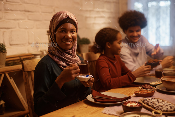 Happy black Muslim mother having cup of tea while gathering with family ...
