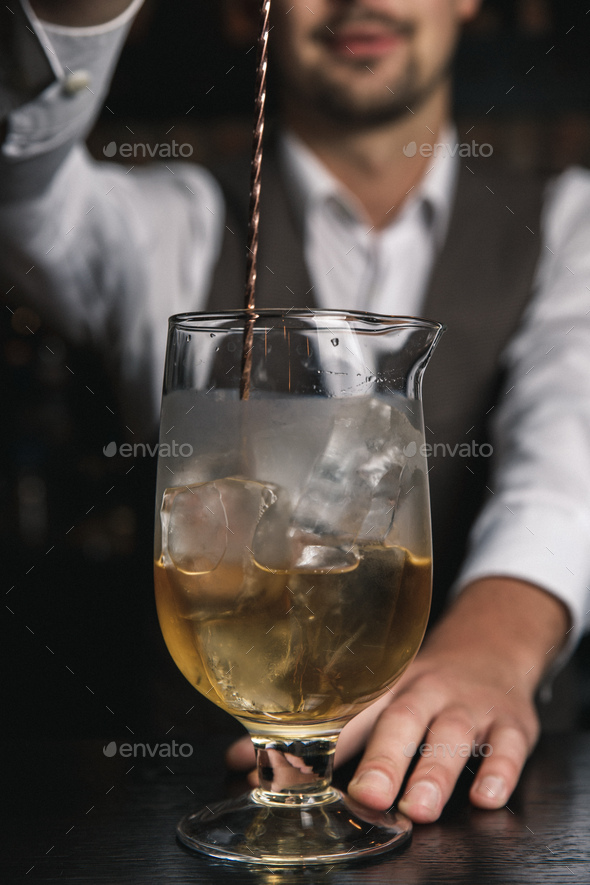 A vertical image of barman's hands stirring up a cocktail with ice ...
