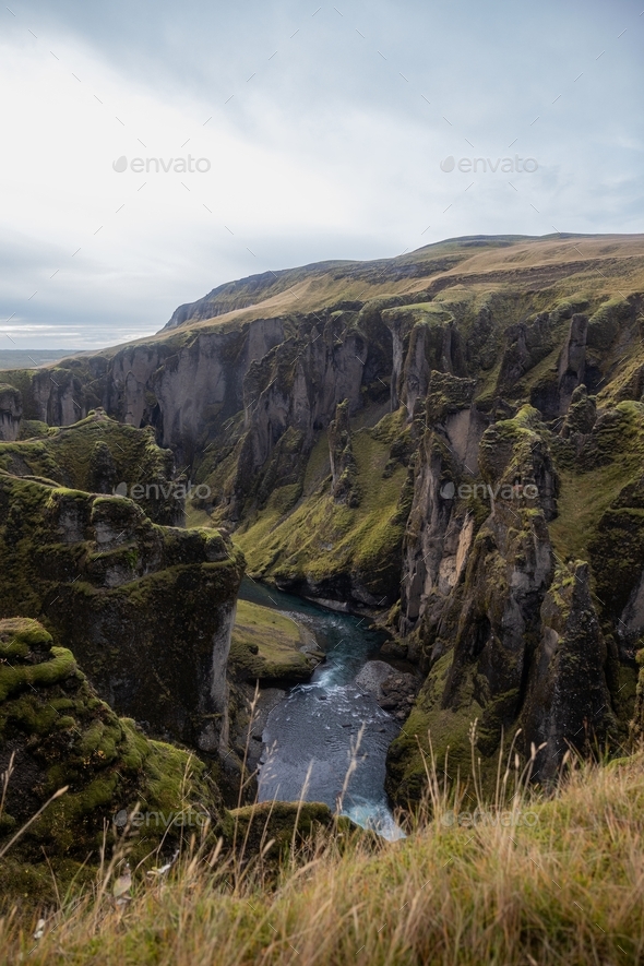 River surrounded by rocks covered in greenery and dry grass under a ...