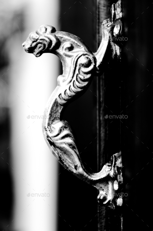 Vertical greyscale shot of a metal door handle with a lion carving ...