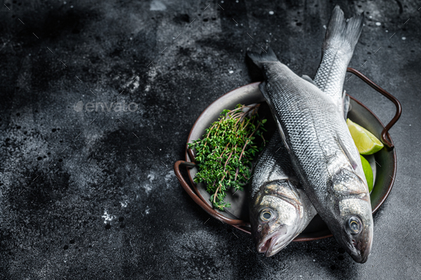 Fresh Raw Sea Bass, Labrax fish with herbs and lime. Black background ...