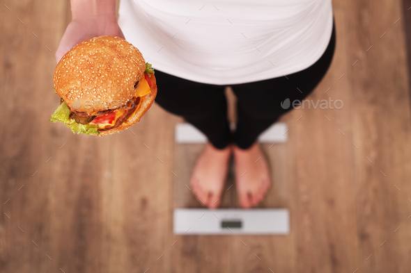 Woman Measuring Body Weight On Weighing Scale Holding Burger Stock ...