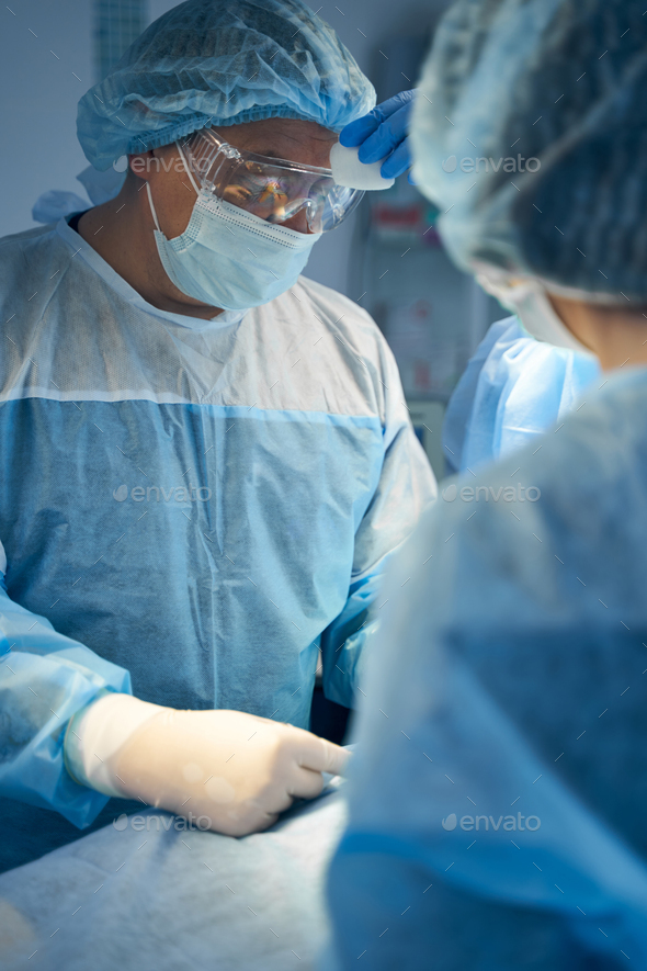 Doctor doing surgery while getting sweat wiped off his head Stock Photo ...