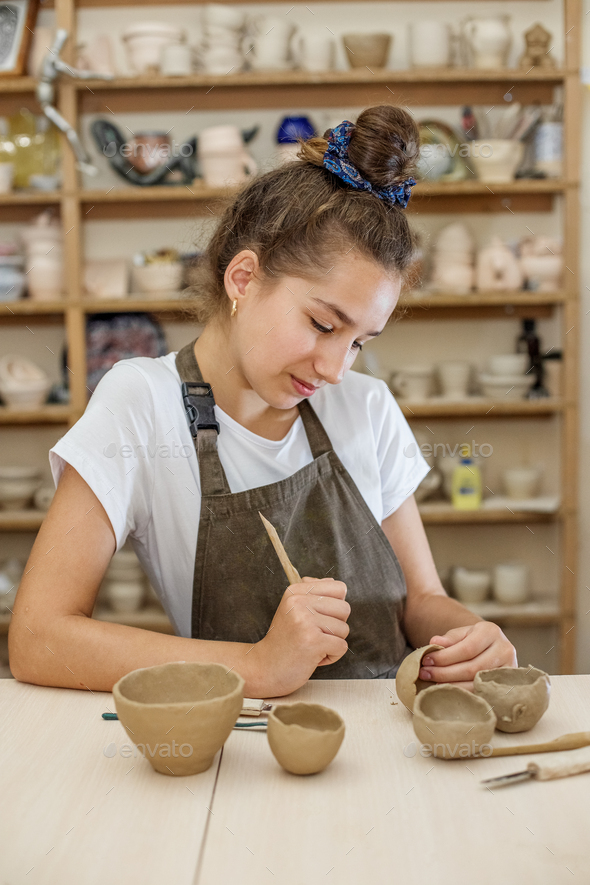 Beautiful teenage girl playing with modeling clay in pottery workshop ...