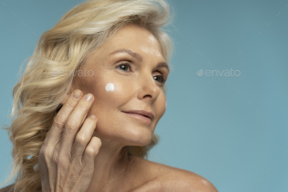 Close-up gorgeous blonde mature woman, applying anti-aging cream on ...