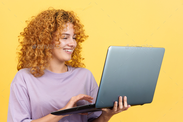 Smiley woman standing and using a laptop Stock Photo by ivanmorenosl