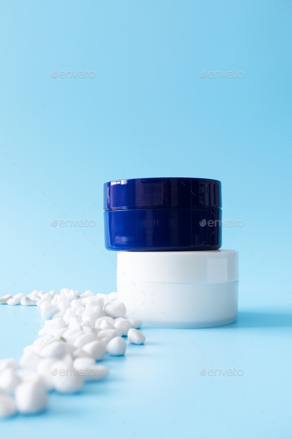 White and blue moisturizer cream jars and small minerals on blue ...