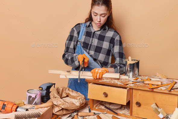 Skilled female carpenter cuts wooden plank with jigsaw produces wooden ...