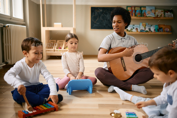 Group of children and their black female teacher playing musical ...