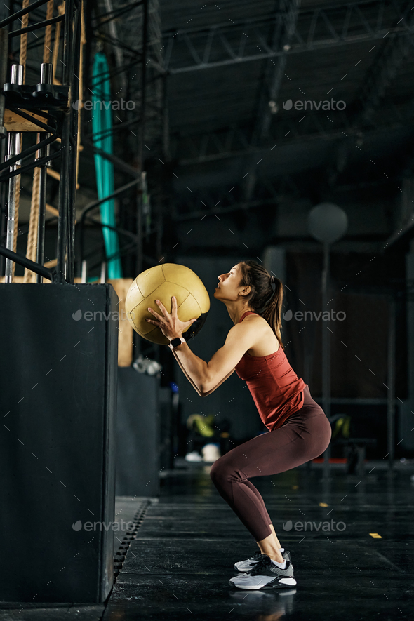 Female athlete doing squat and throw exercise with medicine ball in a ...
