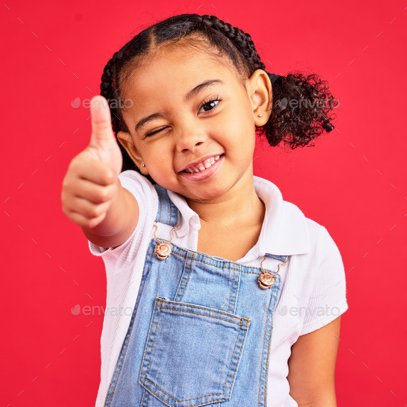 Thumbs up, portrait and girl child in studio, red background or ...