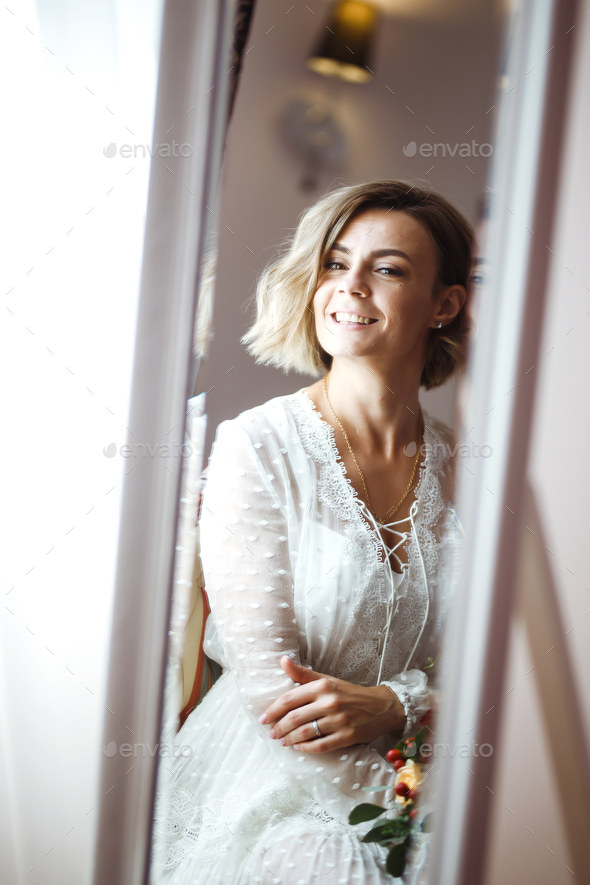 Bride in elegant white dress looking in mirror. The bride smiles and ...