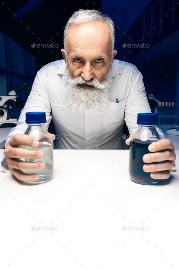 portrait of evil scientist with bottles with reagents looking at camera ...