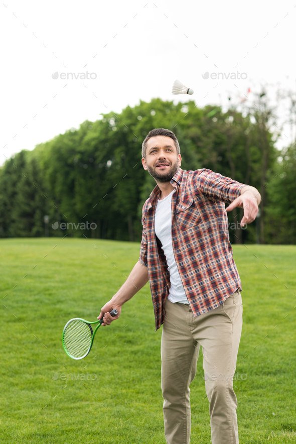 happy active man playing badminton with racquet and shuttlecock in park ...
