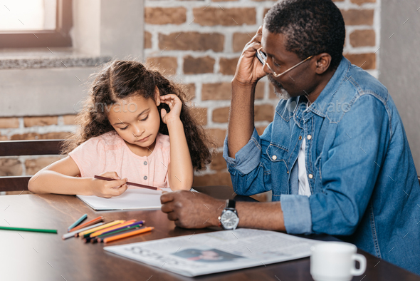 African american man helping his daughter drawing picture with colorful ...