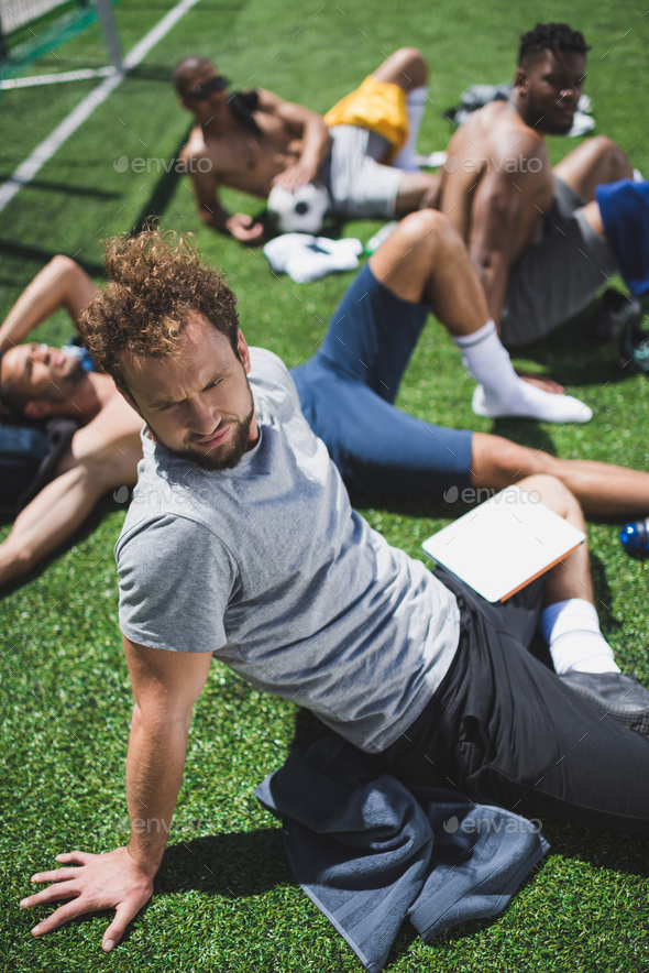 group of multiethnic soccer players resting on football field after ...