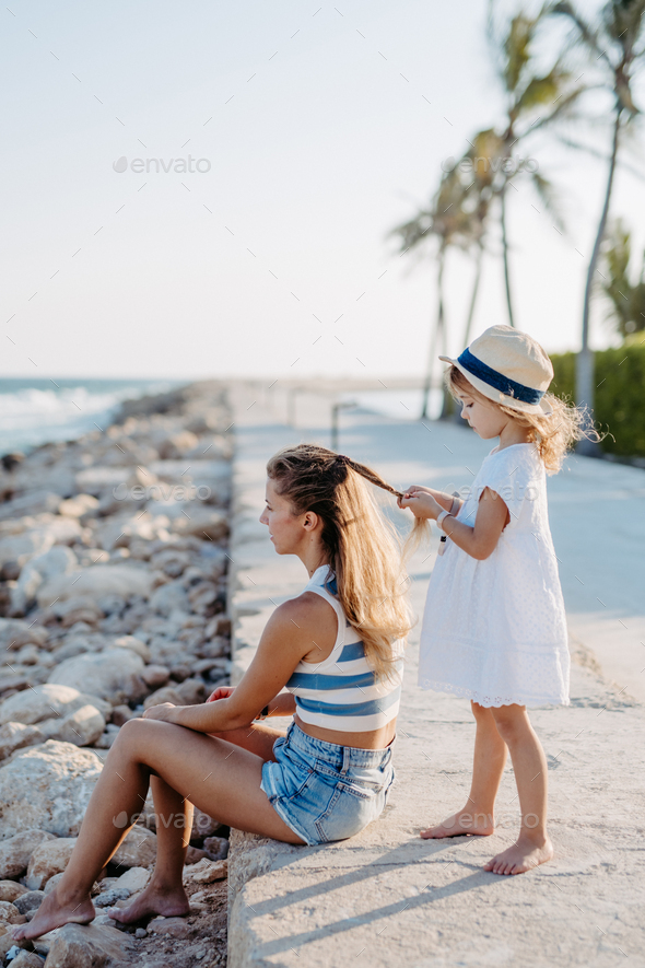 Little girl making hairstyle her mother, enjoying summer time at sea ...
