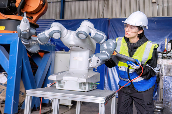 Young female asian service engineer holding robot controller operate robot arm automation ...