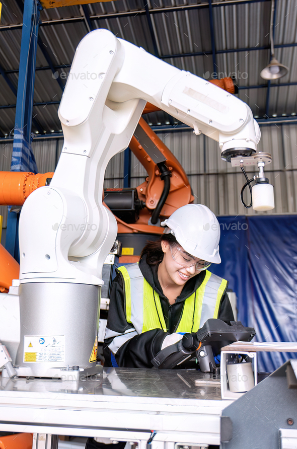 Young female asian service engineer holding robot controller operate robot arm automation ...