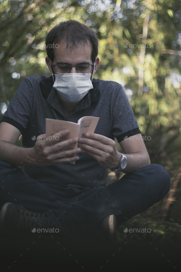Man sitting on a rock reading a booklet and wearing a facemask on a ...