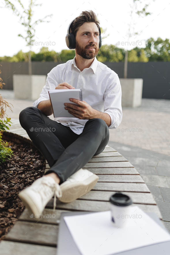 Man writing in notepad while sitting on bench with legs Stock Photo by ...