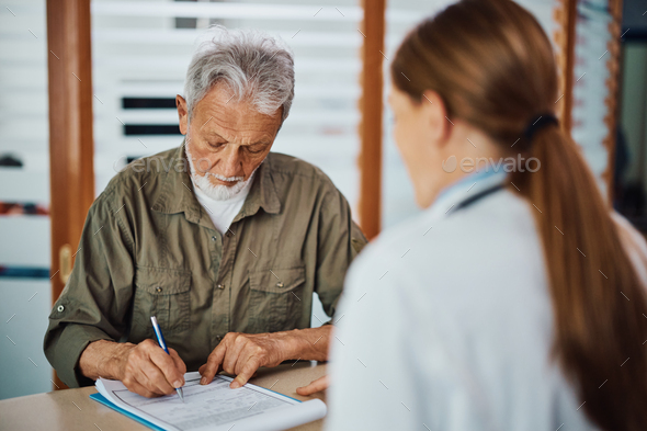 Senior man filling medical paperwork at reception desk at doctor's ...