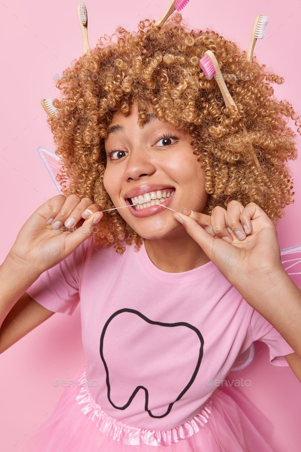 Vertical shot of positive curly haired woman cleans teeth with dental ...