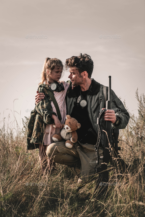 handsome man holding gun near kid with teddy bear in field, post ...
