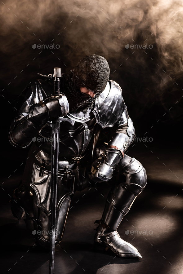 handsome knight in armor holding sword and bend knee on black ...