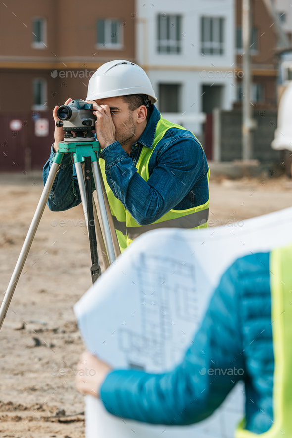 Selective focus of surveyors working with digital level and blueprint ...