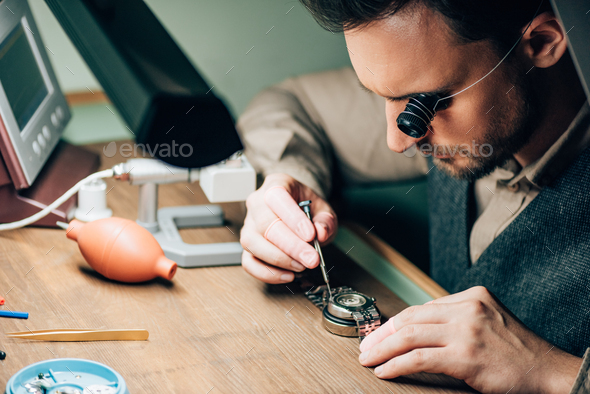 Side view of watchmaker in eyeglass loupe working with wristwatch by equipment on table Stock ...