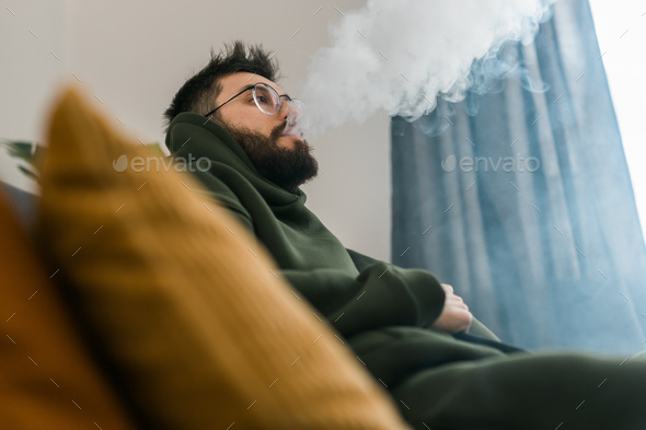Bearded millennial or gen z man smoking hookah while relaxing on sofa ...