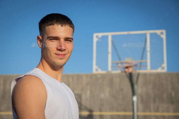 A smiling basketball player on a basketball court with a hoop behind ...
