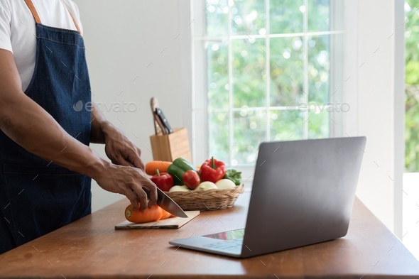 Man in kitchen looking at recipes on laptop while cooking Stock Photo ...