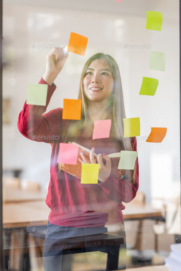 Asian businesswoman creating project plan on office wall with sticky ...