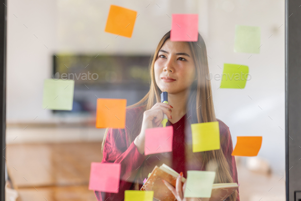 Asian businesswoman creating project plan on office wall with sticky ...