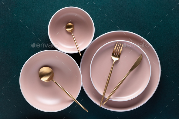 Crockery and golden cutlery on a dark green background, table top view ...