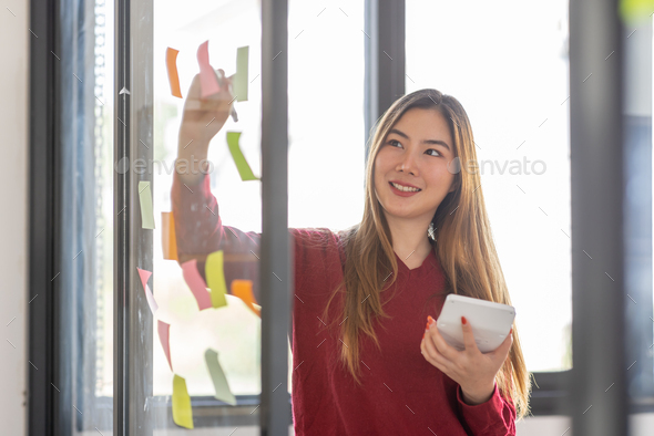 Asian businesswoman creating project plan on office wall with sticky ...