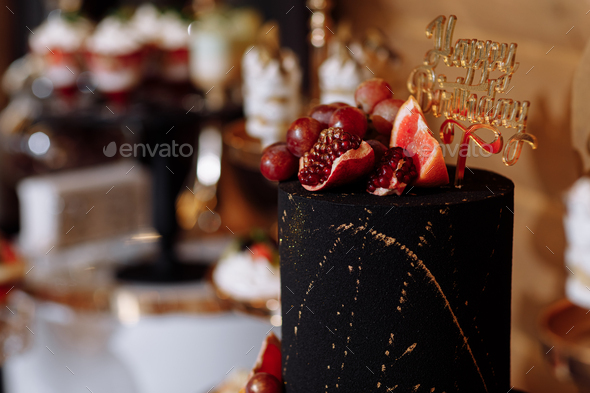 big black birthday cake with fresh fruits and sweets on a festive table ...
