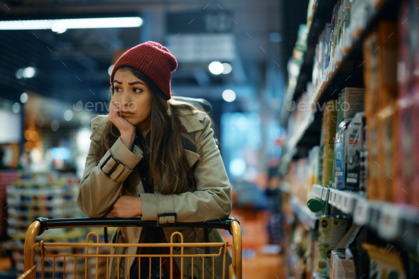 Young sad woman with empty shopping cart among produce aisle at ...