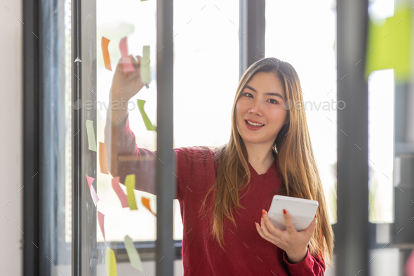 Asian businesswoman creating project plan on office wall with sticky ...