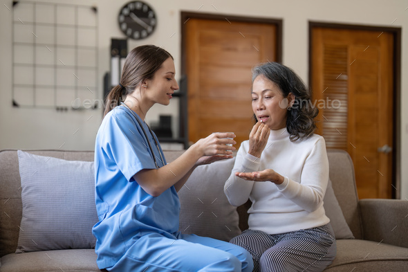 Contented senior woman taking medicines while her caregiver advising ...