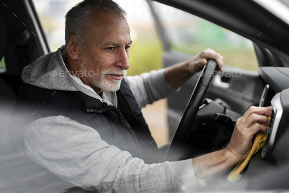 Handsome senior man sitting on the driver's seat, using microfiber ...