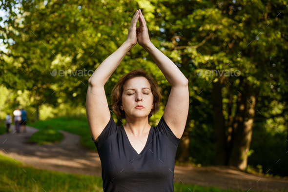 adult woman meditates with folded palms in the park with closed eyes ...