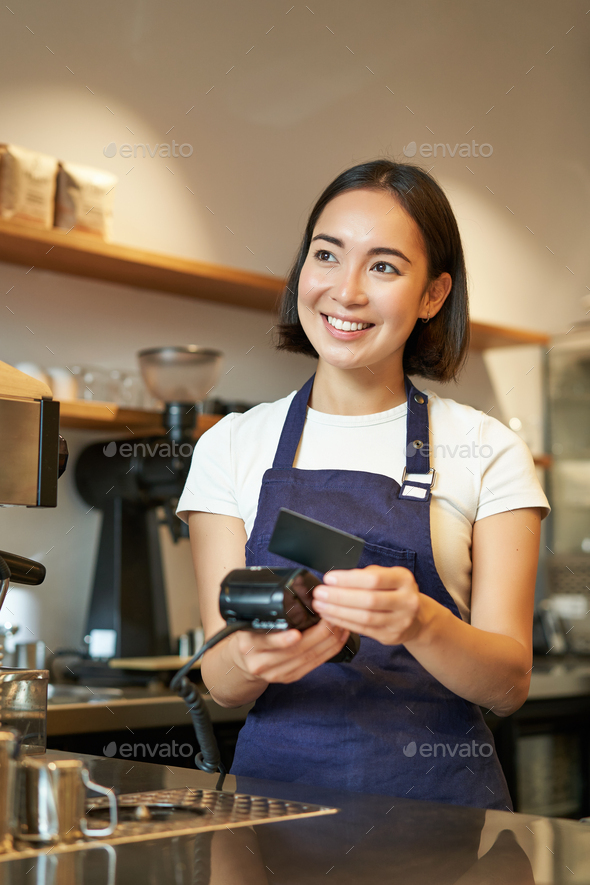 Portrait of smiling asian barista, coffee shop employee using POS ...