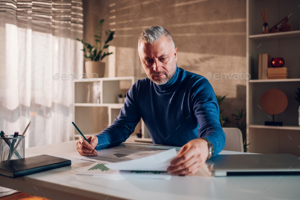 Gray haired middle aged man working in a home office with work ...